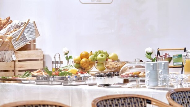 Disposição de buffet de café da manhã com diversos tipos de comida e uma mesa com cadeiras.