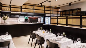 Um restaurante com mesas postas para refeições, um espaço de recepção e um bar.