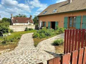Uma trilha pavimentada que leva a uma casa com telhado inclinado e persianas verdes.