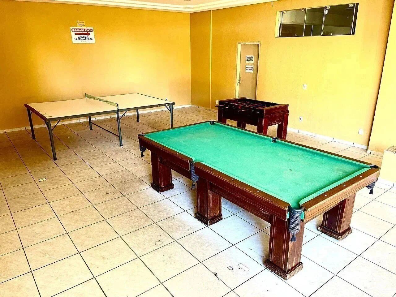 Uma sala de jogos com mesa de bilhar, duas mesas de futebol de mesa e uma mesa de tênis de mesa.