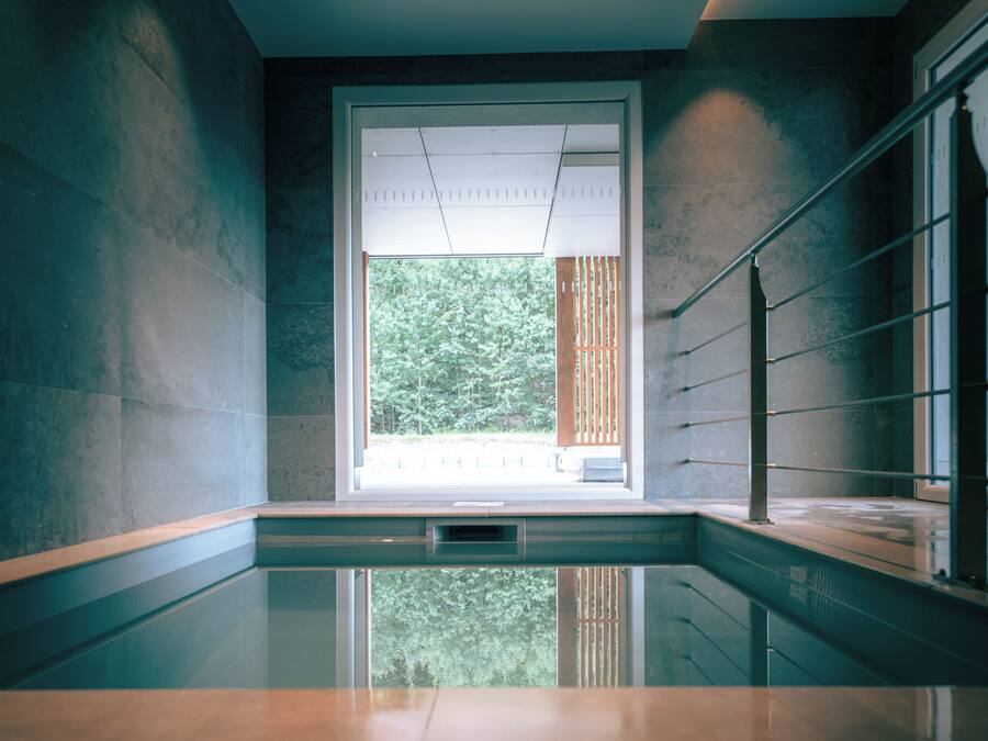 Um interior moderno com uma piscina refletora, uma janela grande com vista para o verde e um guarda-corpo de metal.
