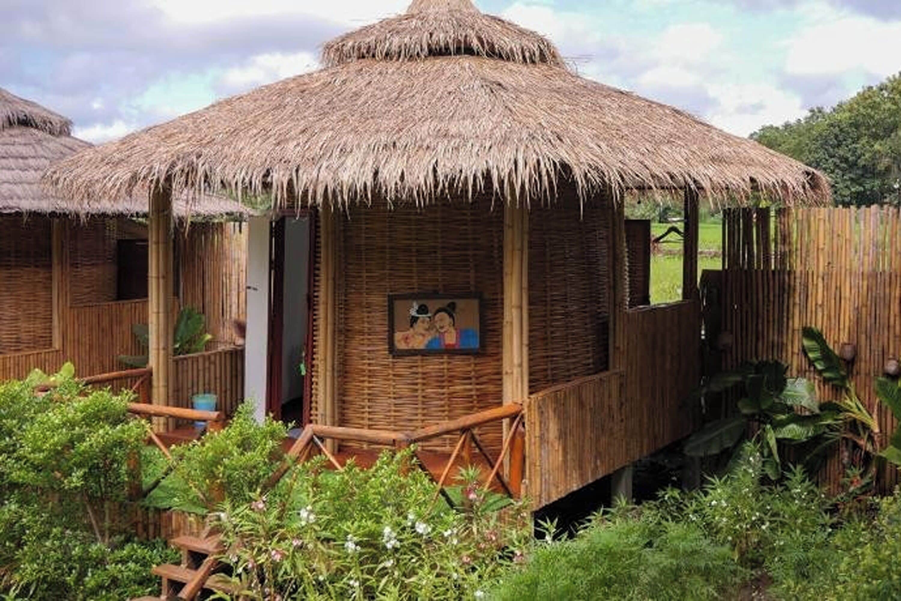 Uma cabana com telhado de palha, varanda de madeira e um quadro na parede.