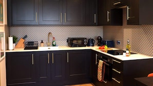 Cozinha moderna com armários escuros, painel de fundo decorado e diversos eletrodomésticos, incluindo micro-ondas e máquina de café.