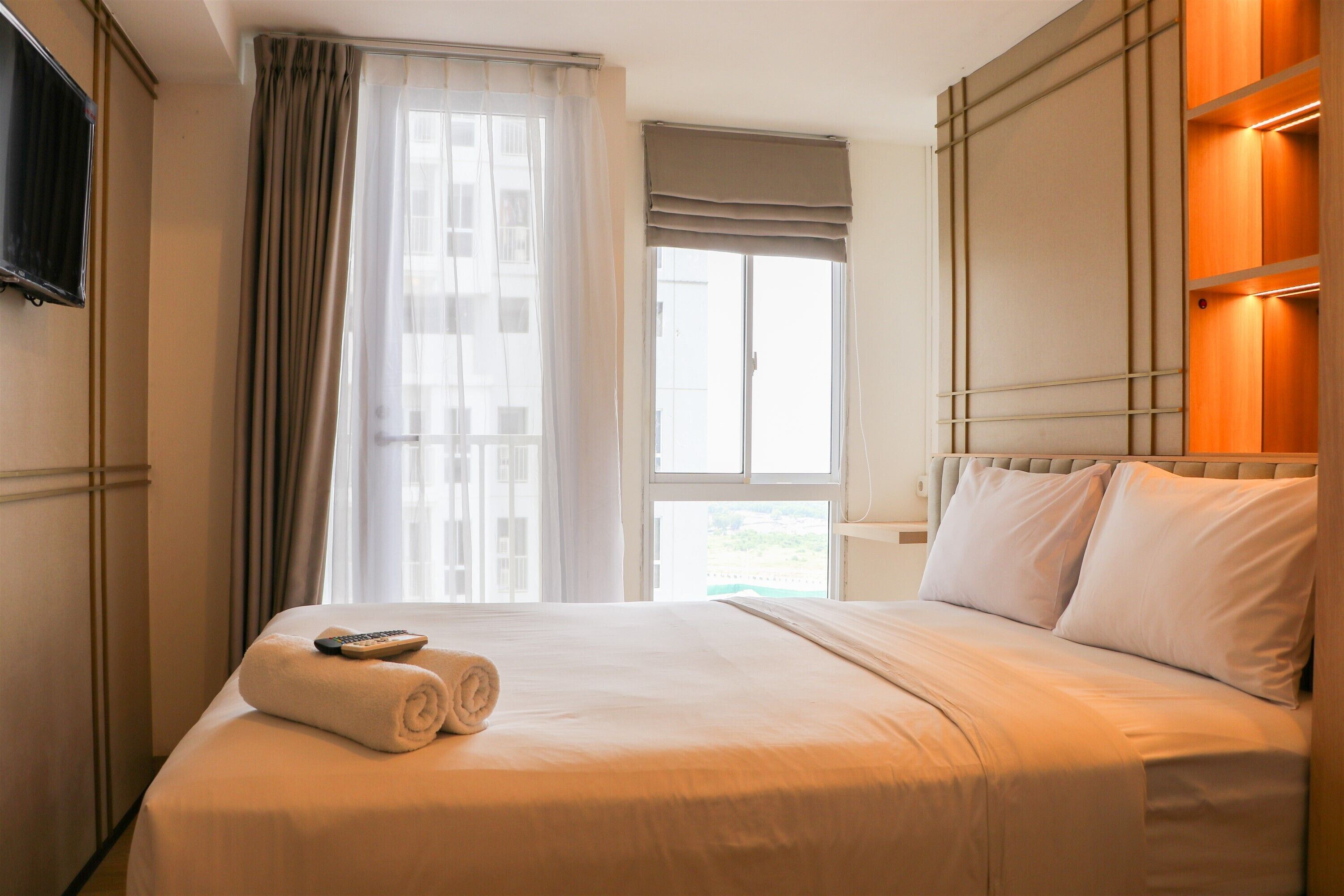 Quarto de hotel com uma cama grande, televisão fixada na parede e janela com cortinas.