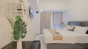 Quarto de hotel moderno com cama, mesa de cabeceira, televisão e uma planta em vaso.