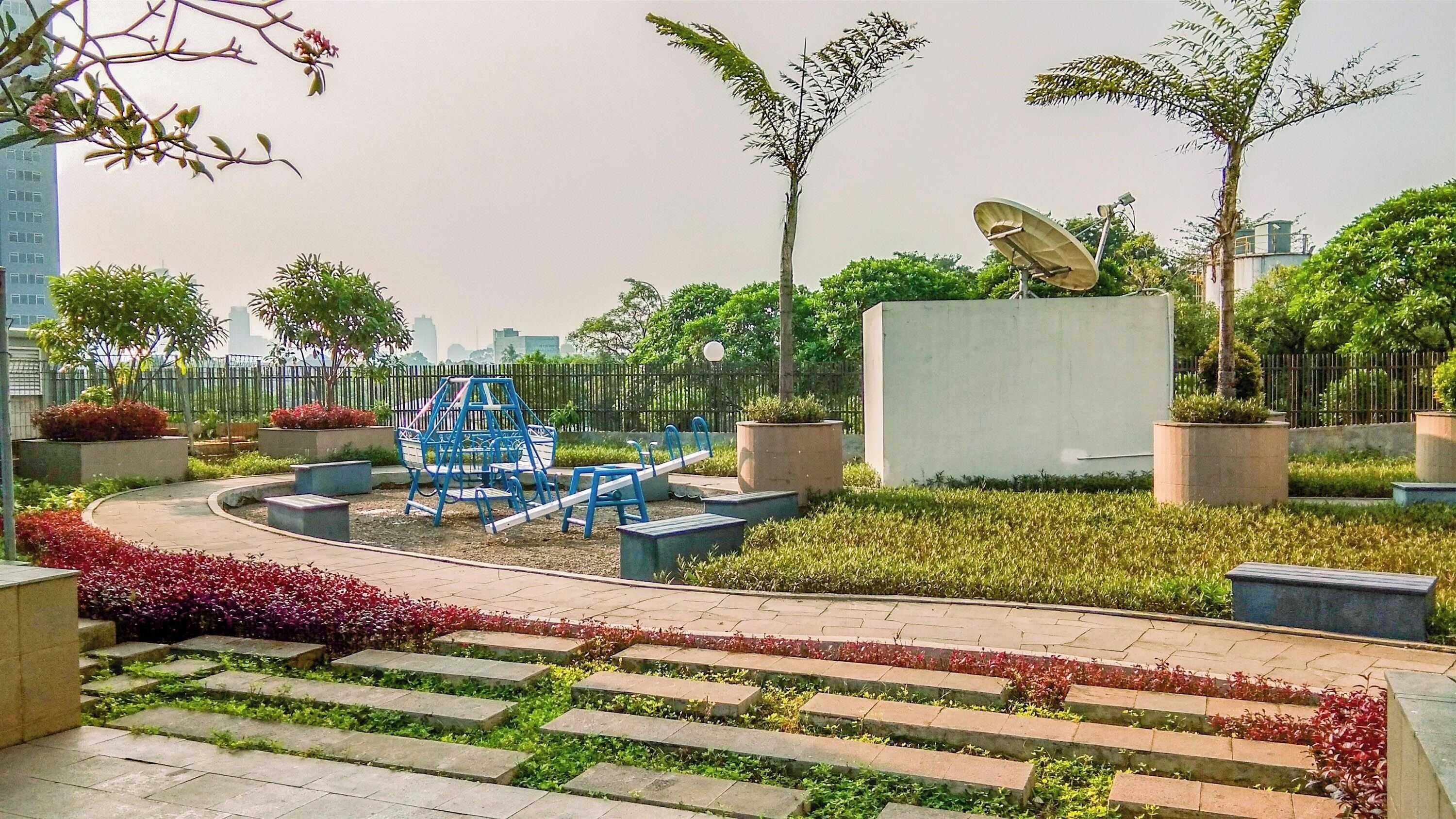Um parque com equipamentos de playground, uma antena parabólica grande e um muro de concreto.