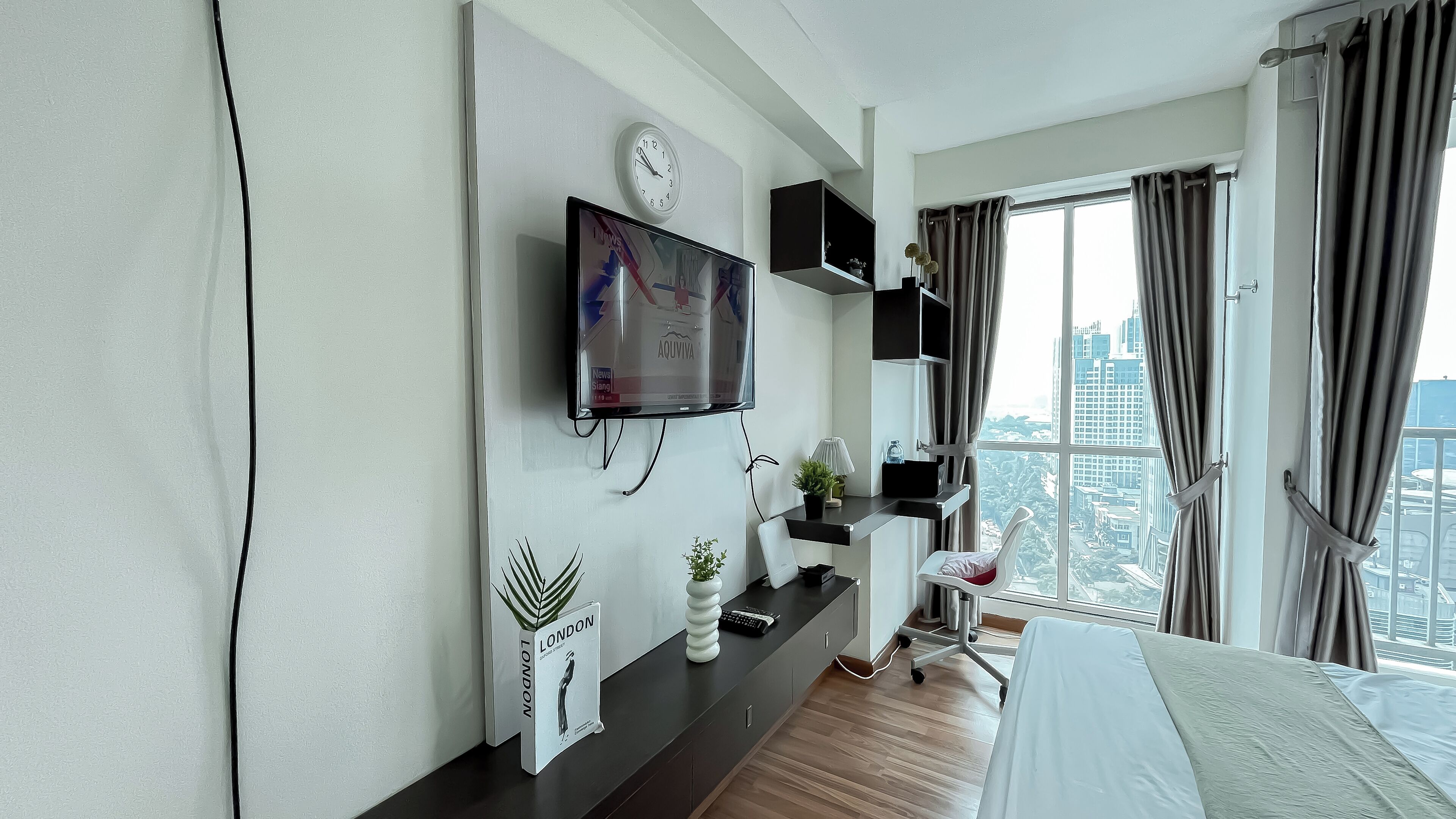 Quarto de hotel moderno com uma janela grande, uma cama, televisão fixada na parede e uma pequena área de trabalho.