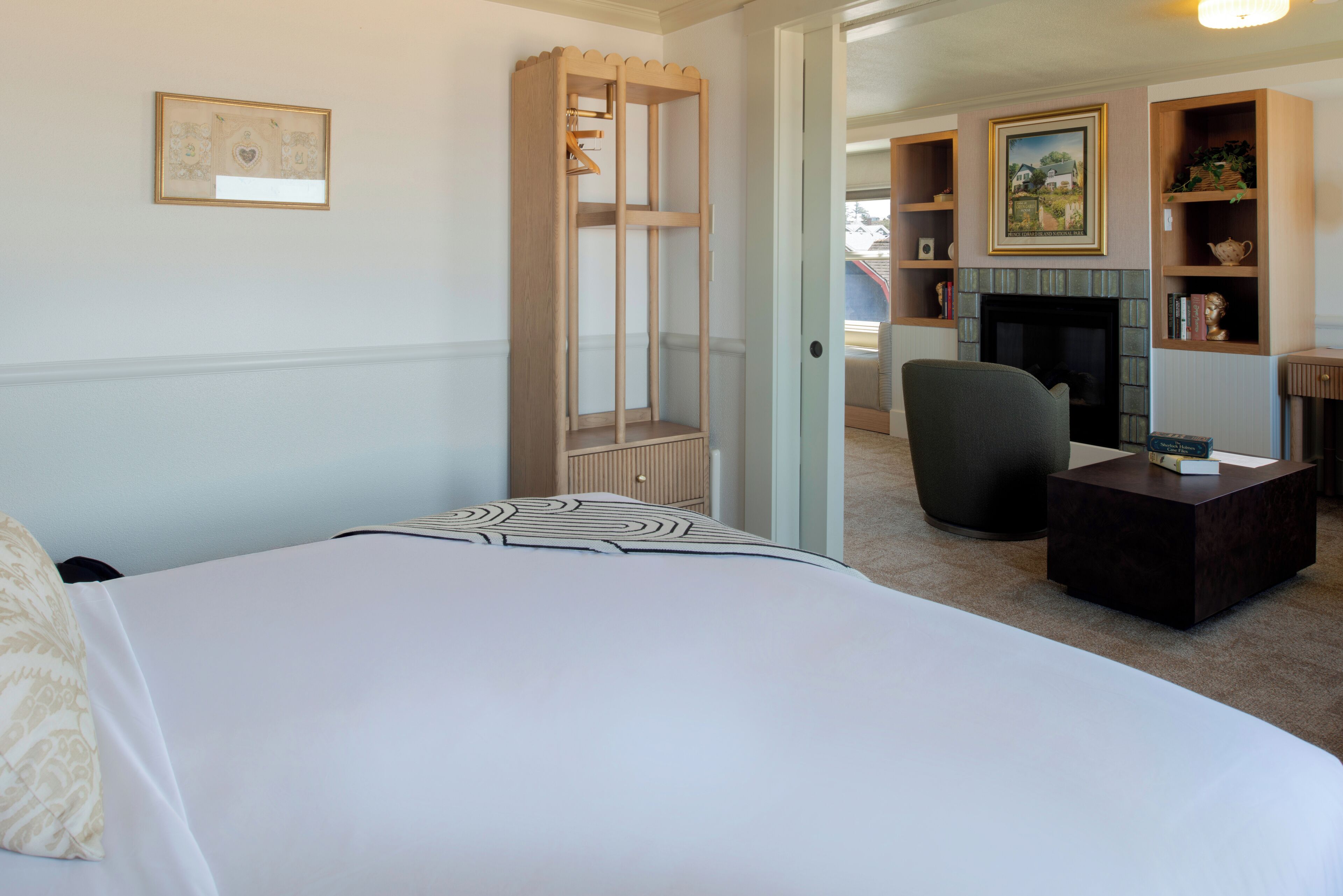 Um quarto com uma cama grande, um guarda-roupa de madeira, lareira e um espaço de estar com uma cadeira e uma mesa pequena.