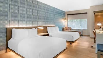 Quarto de hotel com duas camas, uma escrivaninha e uma janela com vista para o verde.