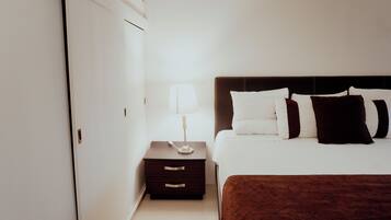 Quarto de hotel com cama, mesa de cabeceira com abajur e guarda-roupa.