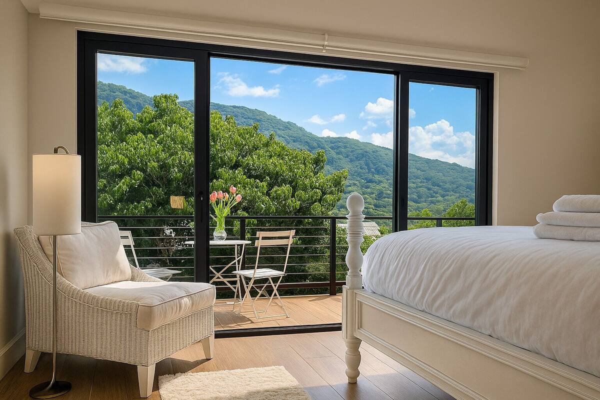 Quarto com uma janela grande, uma cama, uma cadeira e uma mesinha.