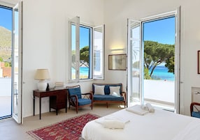 Quarto com cama, escrivaninha, cadeira, tapete e janelas amplas com vista para o mar.