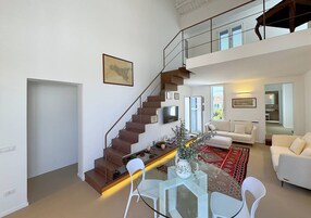 Ampla sala de estar com escada, sofá, mesa de centro e mesa de jantar.
