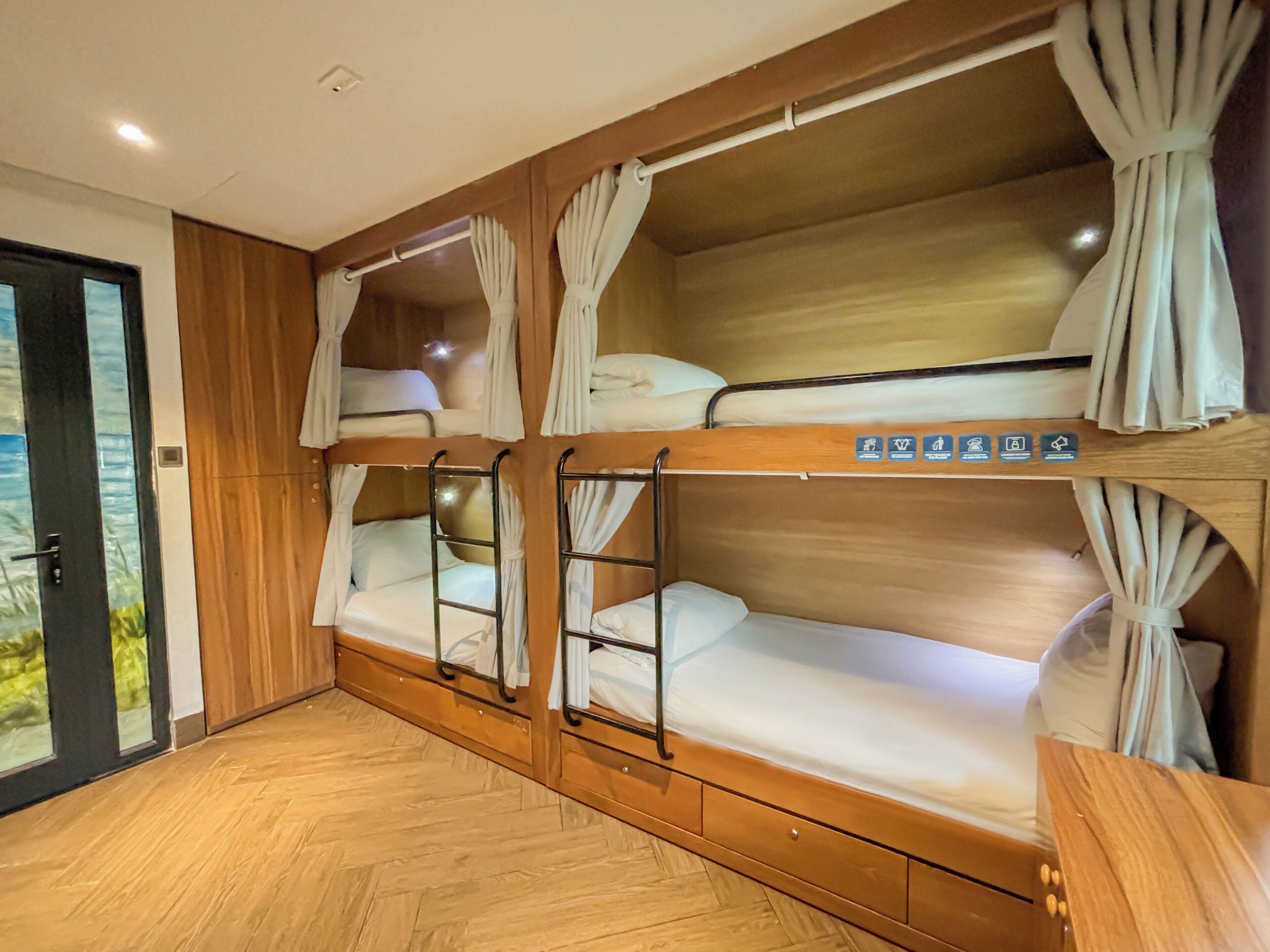 Quarto com beliches, piso de madeira e porta com vista.