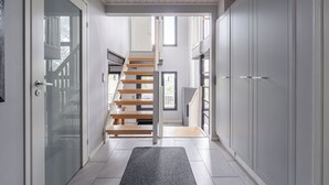 Um interior moderno com uma escada que leva a uma varanda, paredes brancas e uma porta com vidro fosco.