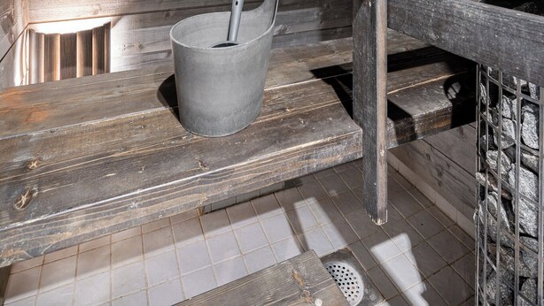 Uma sauna de madeira com um balde de metal e um banco de madeira.