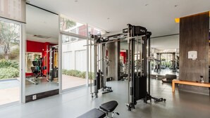 Uma academia com diversos equipamentos de exercício, grandes janelas e um banco.