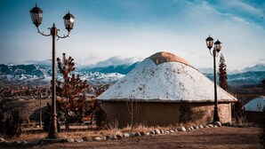 Uma yurta tradicional com telhado coberto de neve, rodeada por montanhas e um céu límpido.