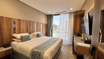 Quarto de hotel com uma cama grande, painéis de madeira, uma mesa com TV e vista para a cidade.