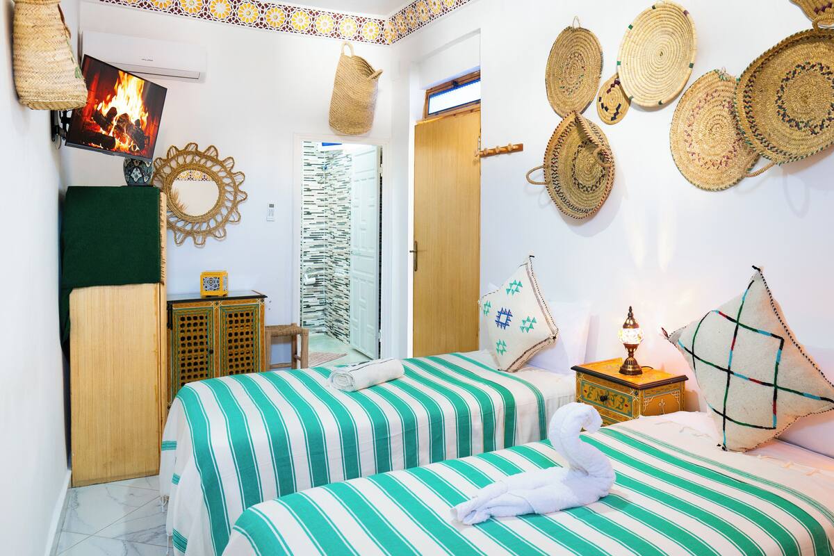 Quarto com duas camas, um guarda-roupa de madeira, um espelho e painéis de parede feitos em tecido.