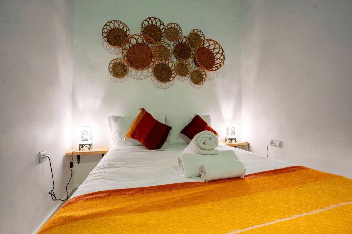 Quarto de hotel com cama, almofadas, cobertor e um enfeite na parede.
