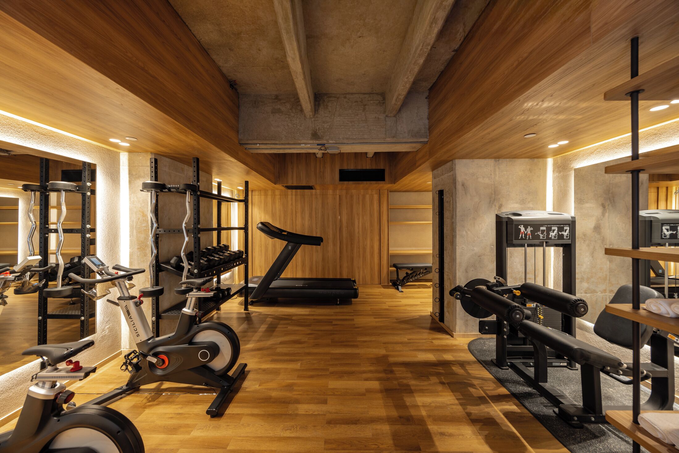 Uma academia com equipamentos de exercício, piso de madeira e teto de concreto.