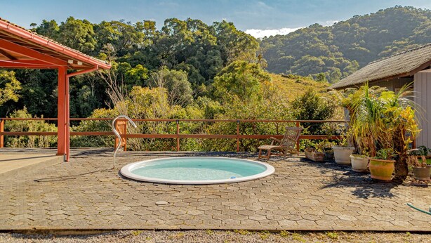 Uma área de piscina com um deck de madeira, uma pérgula vermelha e vista para uma colina arborizada.