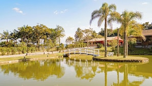 Um lago tranquilo com uma ponte branca, rodeado por vegetação exuberante e um edifício tradicional com telhado vermelho.