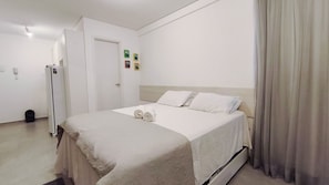Quarto de hotel com uma cama, uma porta, um cesto de lixo e um telefone fixado na parede.