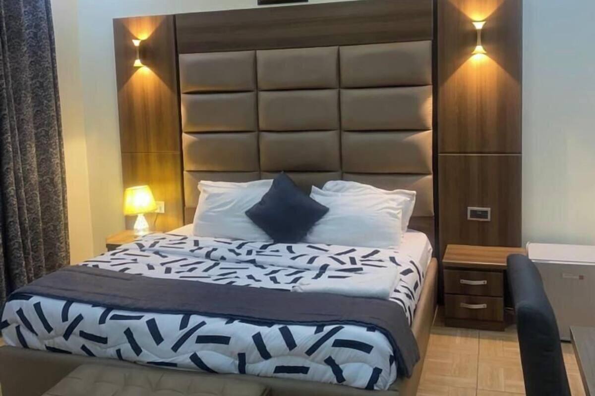 Quarto moderno com uma cama grande, cabeceira de madeira, luminárias de cabeceira, mesa de apoio e uma pequena mesa.