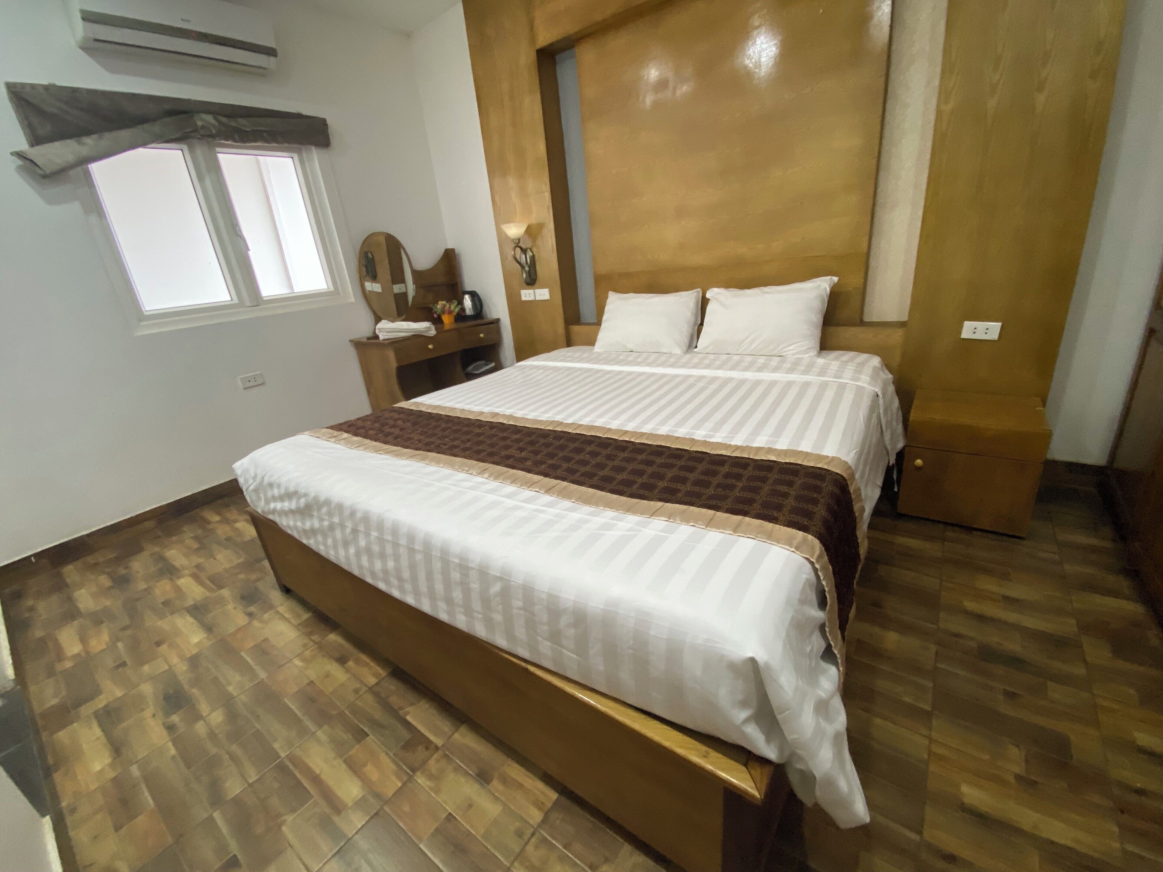 Quarto com cama de madeira, mesa de cabeceira, espelho e janela.