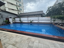 Uma piscina ao ar livre retangular, com borda azulejada e escada de metal.