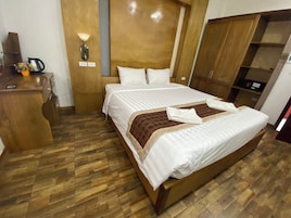 Quarto de hotel bem arrumado com uma cama de madeira, uma escrivaninha com chaleira e um guarda-roupa.