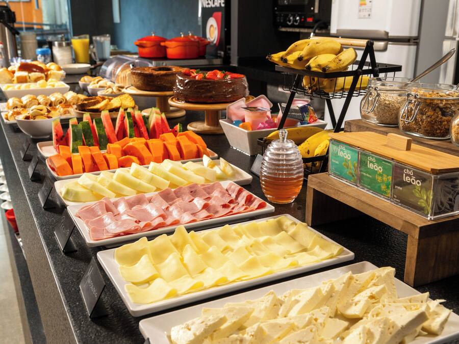 Buffet com diversos alimentos, incluindo carnes, queijos, frutas e um bolo.
