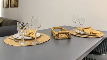 Mesa de jantar posta com dois pratos, duas taças de vinho e uma cesta de fibra.