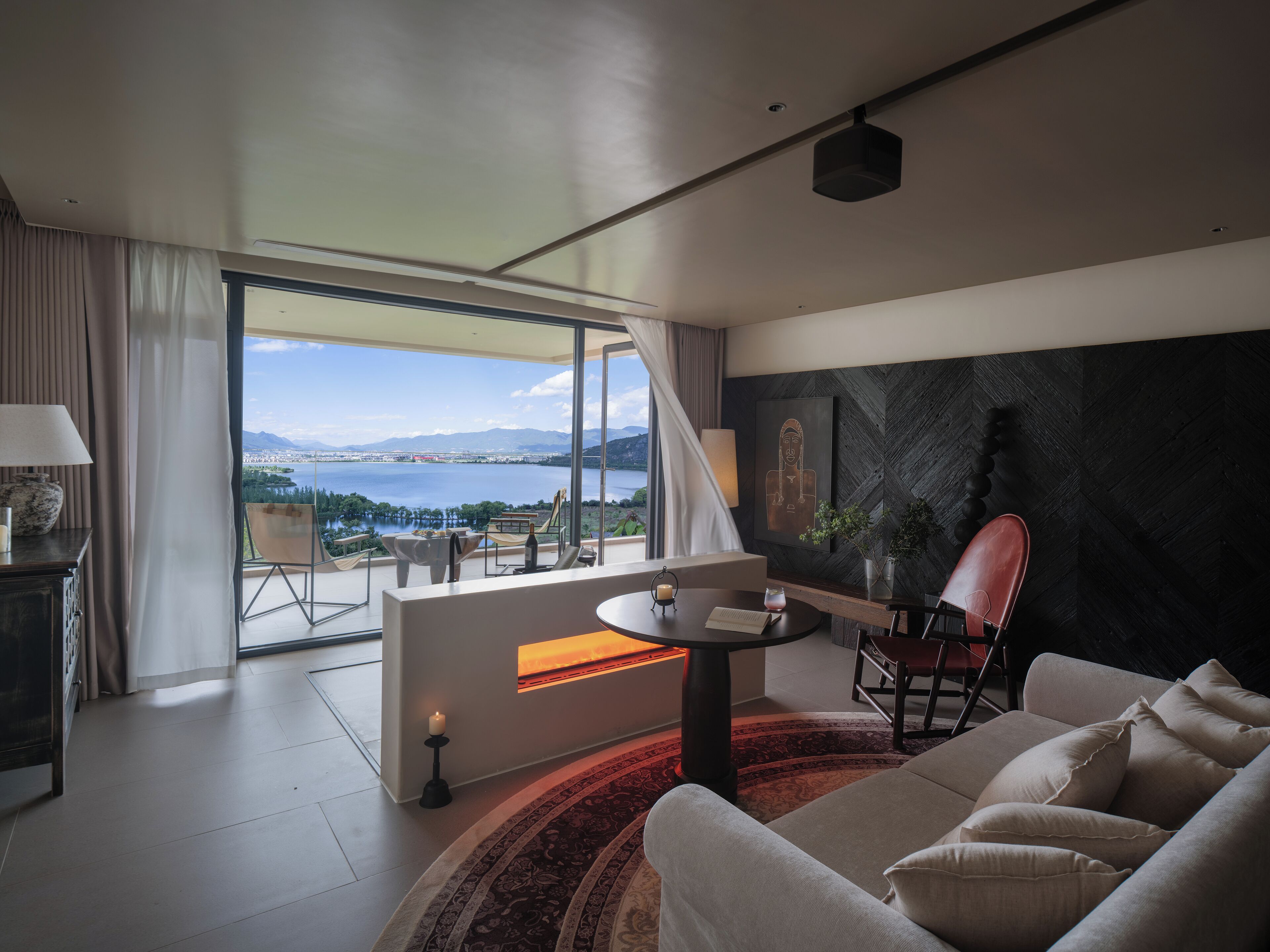 Uma sala de estar moderna com sofá, mesa com vela e vista para um lago e montanhas através de grandes janelas.