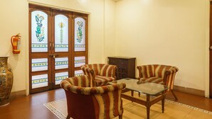 Quarto com mesa de vidro, poltronas com braços listrados, um armário de madeira e uma porta decorativa com painéis de vidro.