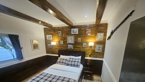 Quarto com cama, mesas de cabeceira, janela com cortinas, painéis de parede de madeira e luminárias fixadas na parede.