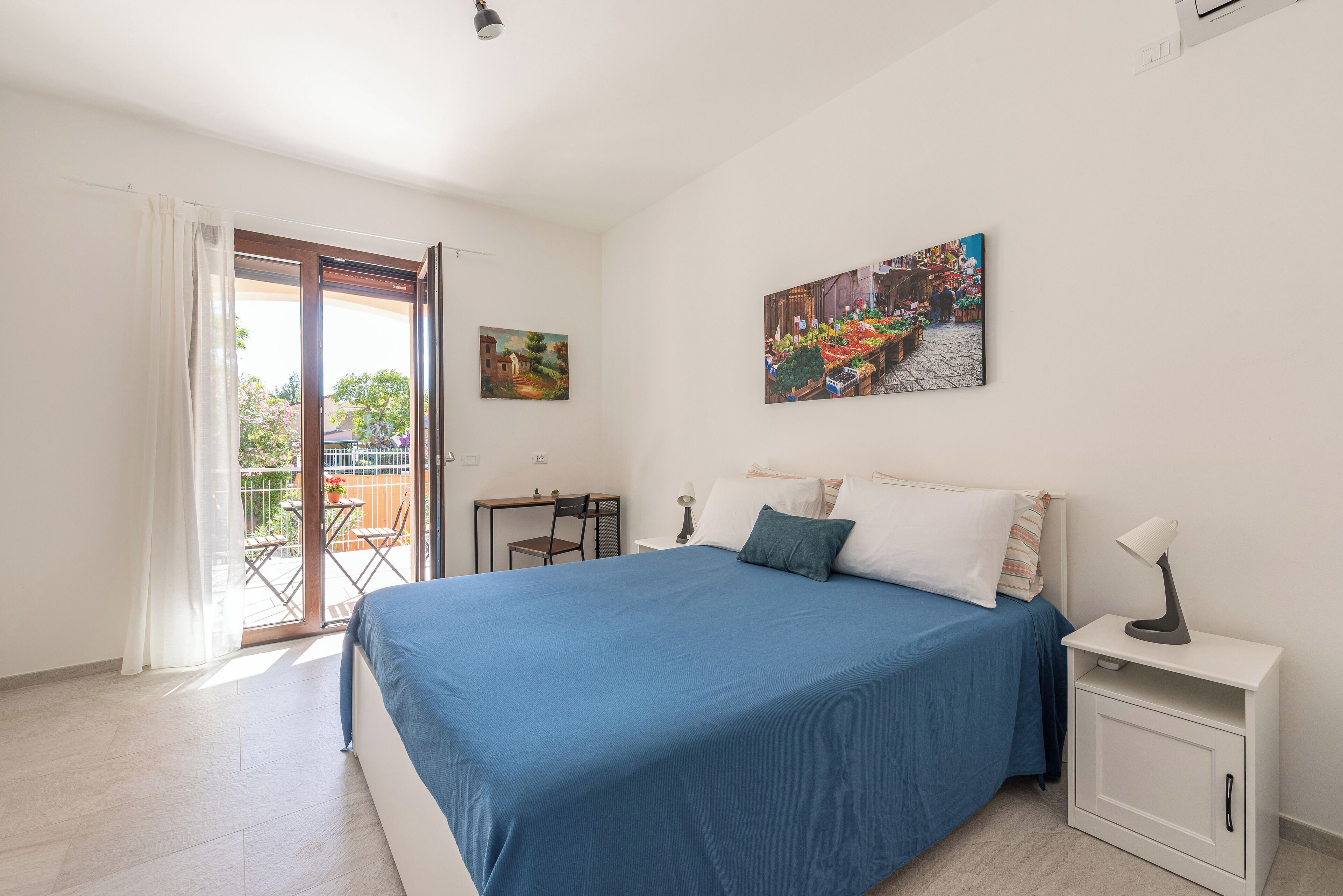 Um quarto com uma cama grande, uma escrivaninha, uma cadeira, uma mesa de cabeceira e um quadro na parede.