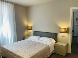 Quarto de hotel com uma cama, duas mesas de cabeceira e duas luminárias fixadas na parede.
