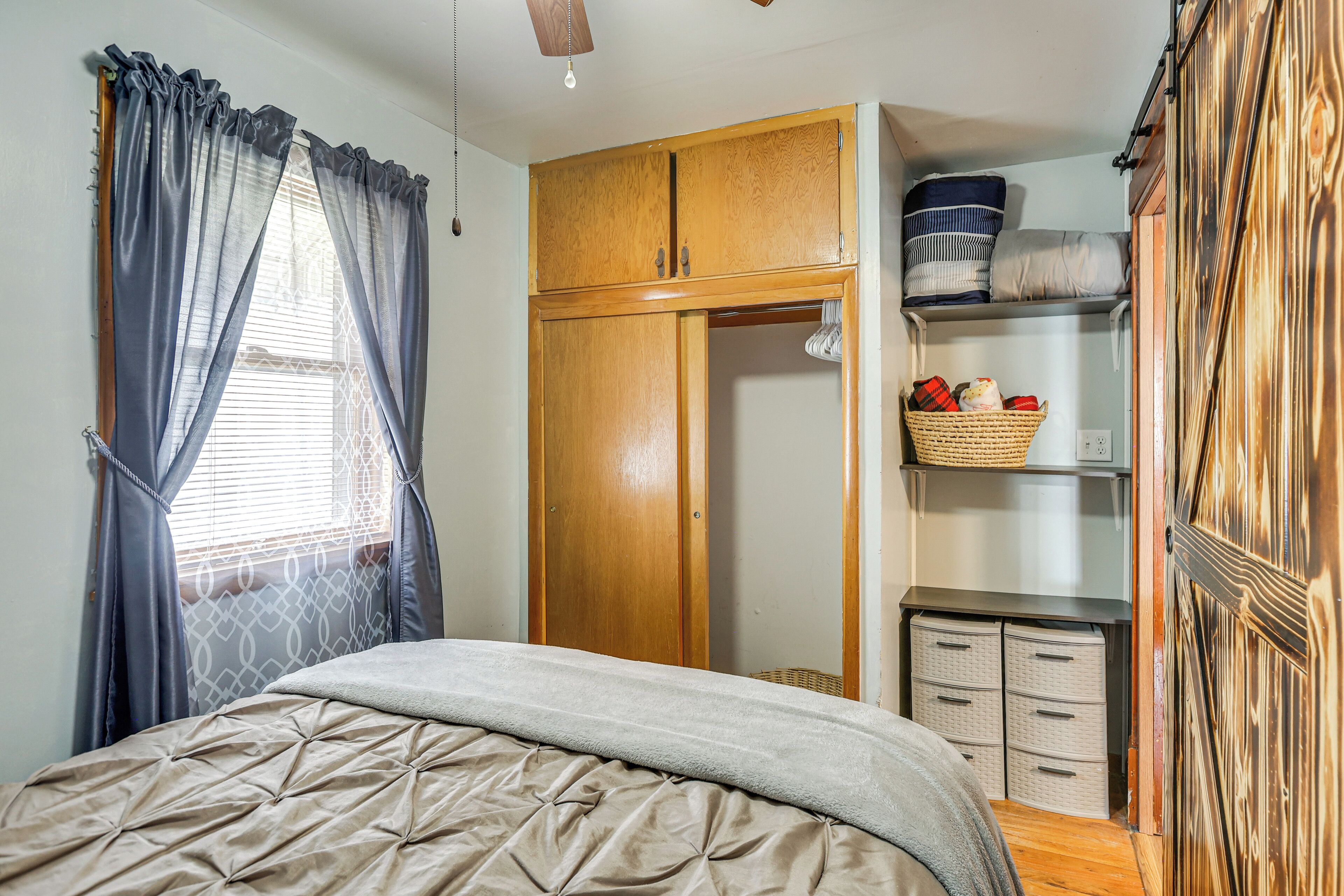 Quarto com cama, guarda-roupa de madeira e estante com cobertores dobrados.