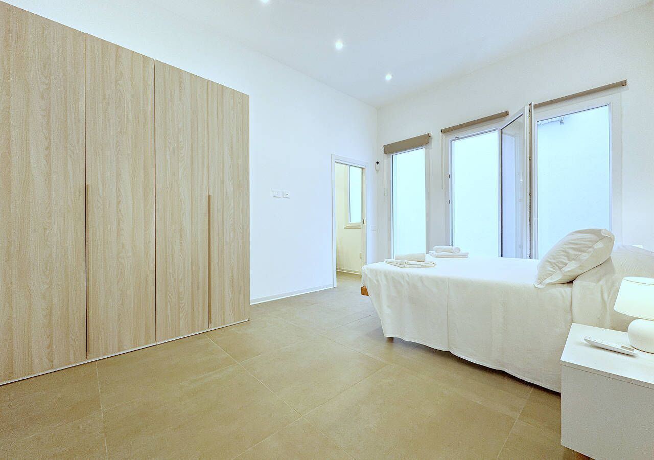 Quarto moderno com guarda-roupa espaçoso, cama com roupa de cama branca e mesa de cabeceira com abajur.
