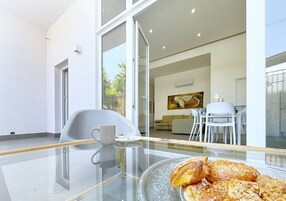 Uma área de refeições moderna com uma mesa de vidro, uma cadeira branca e um prato de comida.