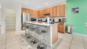 Uma cozinha moderna com armários de madeira, geladeira de aço inoxidável, uma ilha central com banquetas e uma parede verde de destaque.