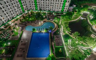 Uma grande piscina rodeada por vegetação, com um pequeno lago e caminhos para passear.