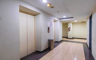 Um corredor com chão de azulejos, uma lixeira e um extintor de incêndio na parede.