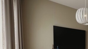 Quarto de hotel moderno com cama, escrivaninha e cadeira, televisão na parede e janela com cortinas.