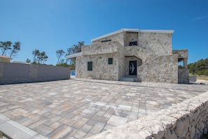 Uma casa moderna de dois andares com fachada de pedra, um acesso pavimentado e um pequeno veleiro atracado na frente.