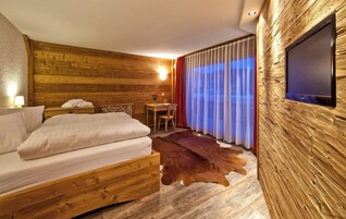 Um quarto com painéis de madeira, uma cama, uma mesinha com um vaso e uma televisão fixada na parede.