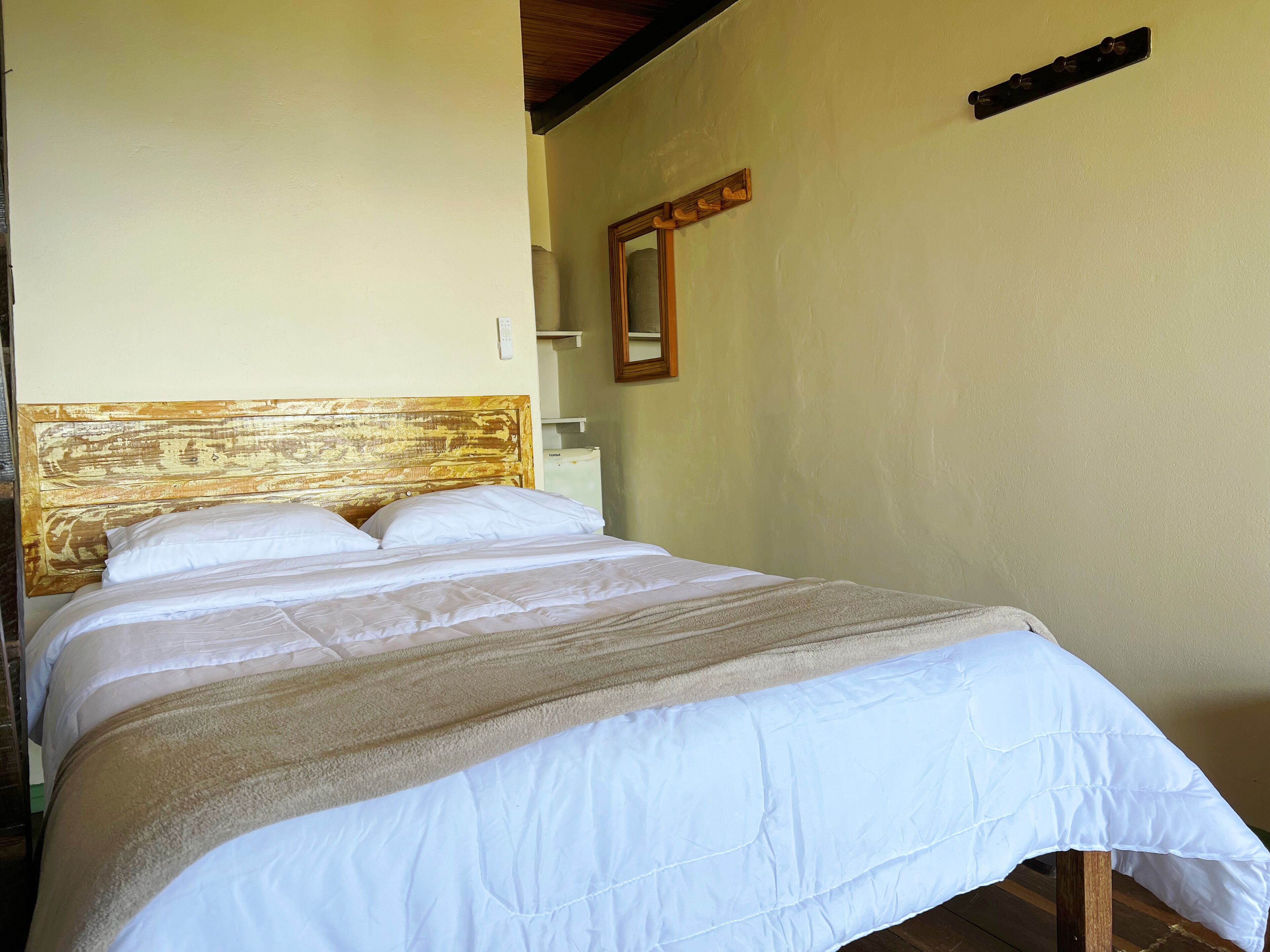 Cama com cabeceira de madeira, roupa de cama branca e manta bege.